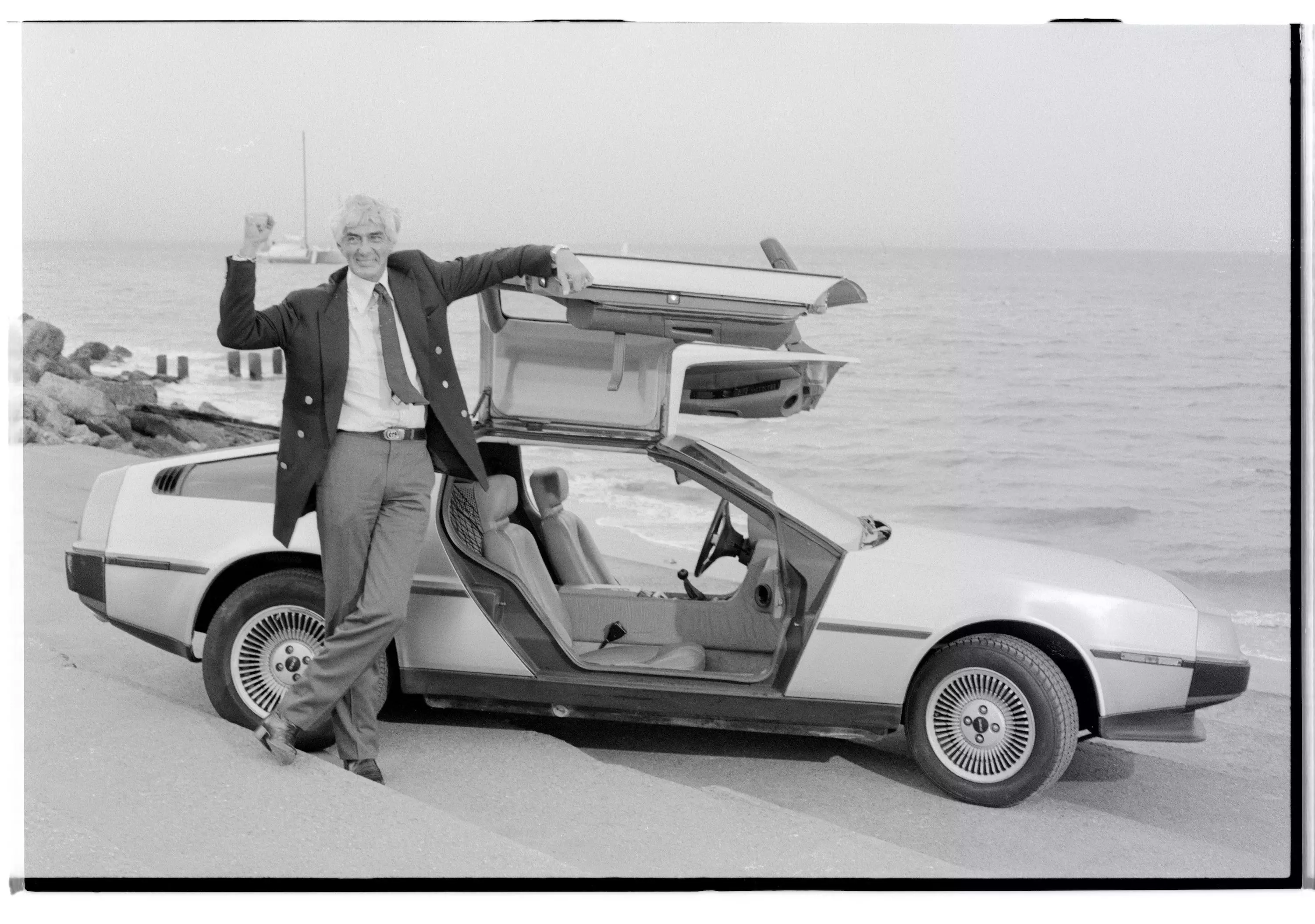 автомобиль эшкуары Джон Делореан үзенең бер спорт машинасы белән Сан-Франциско култыгы янындагы пляжда фотога төшә